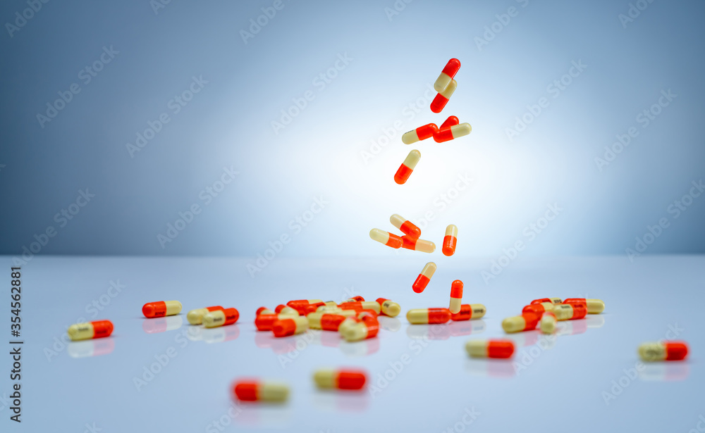 Yellow-orange capsules pill falling down on white table. Pharmaceutical ...