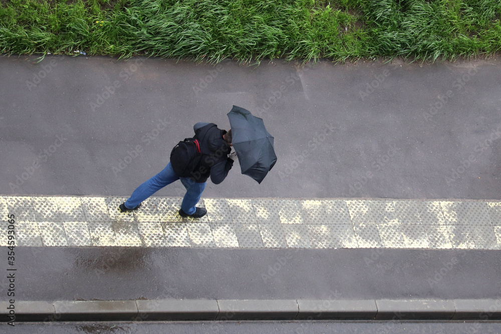 Rain in a city, man with umbrella running on wet sidewalk, top view ...