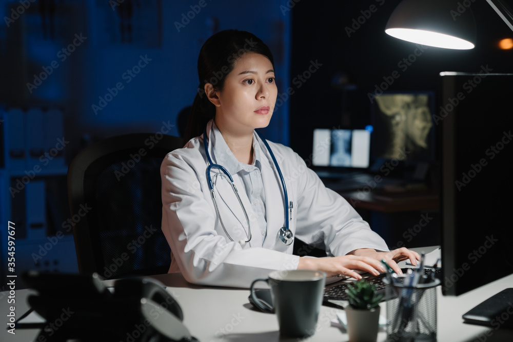 Displeased asian chinese healthcare worker using computer and reading an e-mail at doctor office ...
