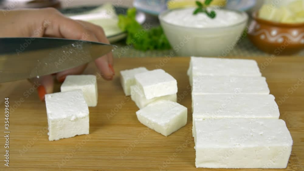Closeup shot of woman hands cutting fresh paneer on a wooden chopping ...