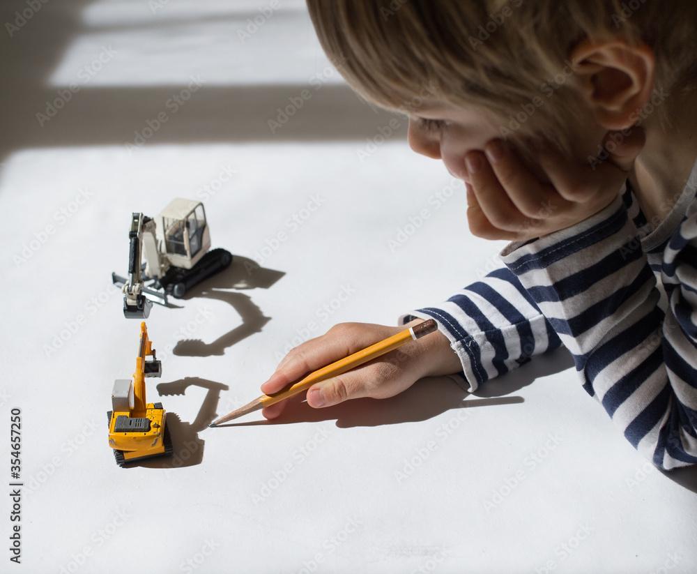 child draws pencil around contrasting shadows from mini metal models of ...