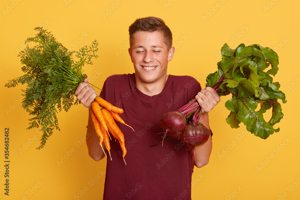 Happy smiling male holding fresh carrot and beets, guy looks satisfied ...