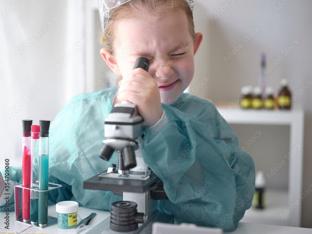 Cute little girl looking into microscope at his desk at home. Young ...
