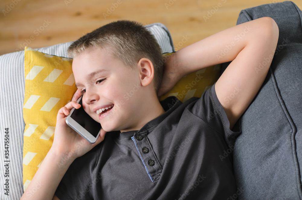 Young teen boy uses cell phone and relaxed at home. A happy blonde boy ...