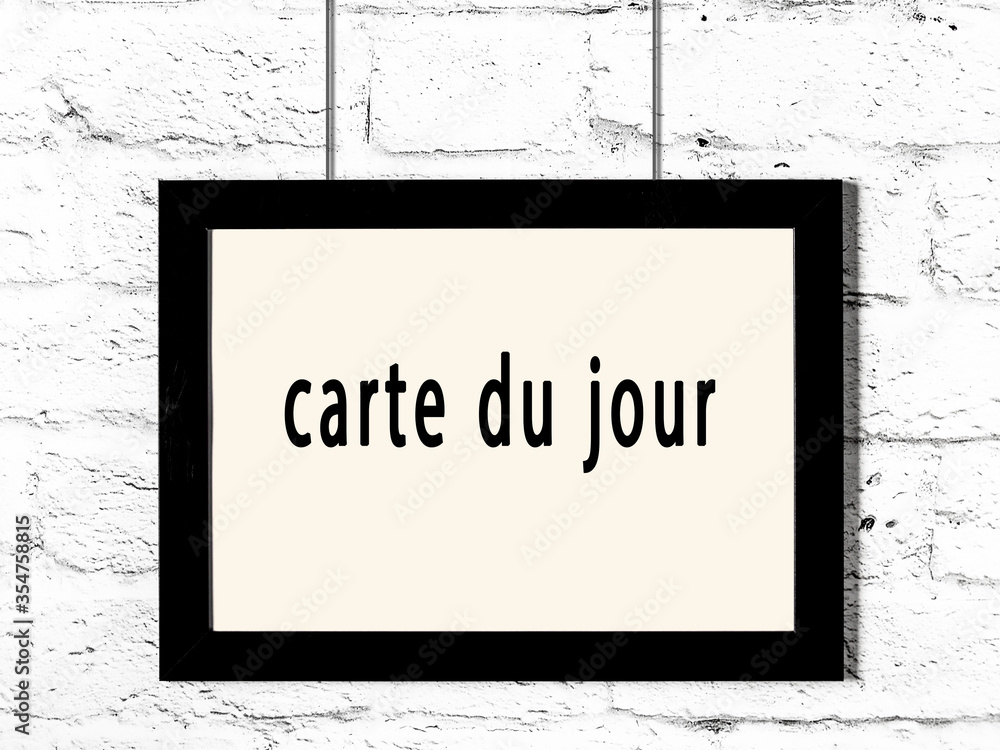 Black frame hanging on white brick wall with inscription carte du jour ...