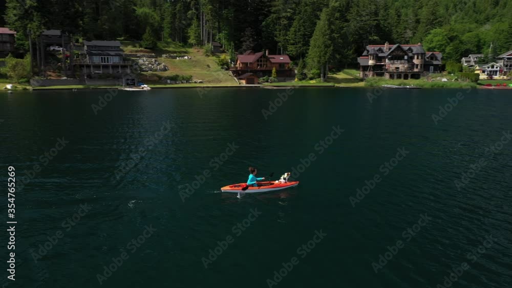 Young woman and her dog rowing a canoe on the water with a view of lake ...