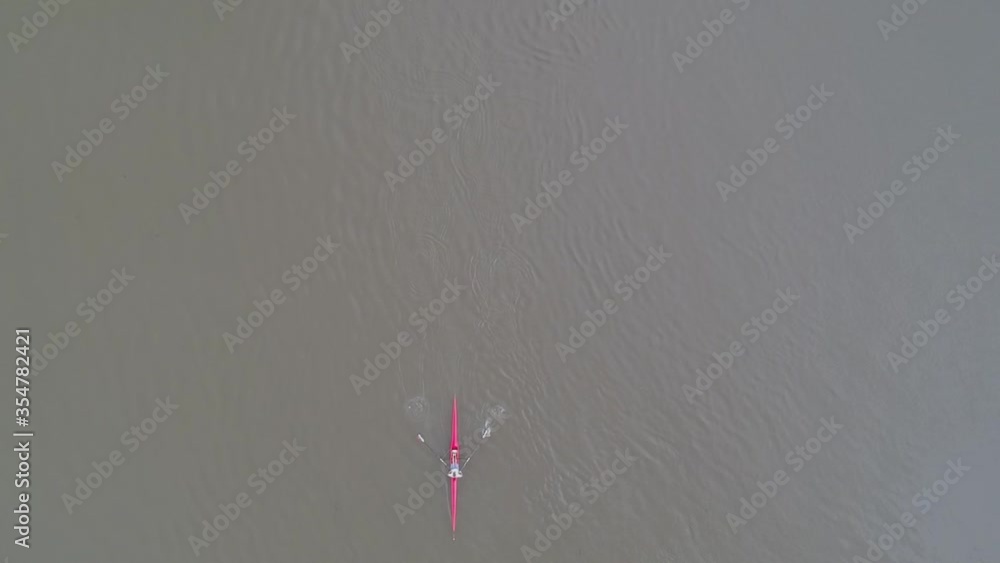 Birds eye view of rower in red canoe rowing from top to bottom of frame ...