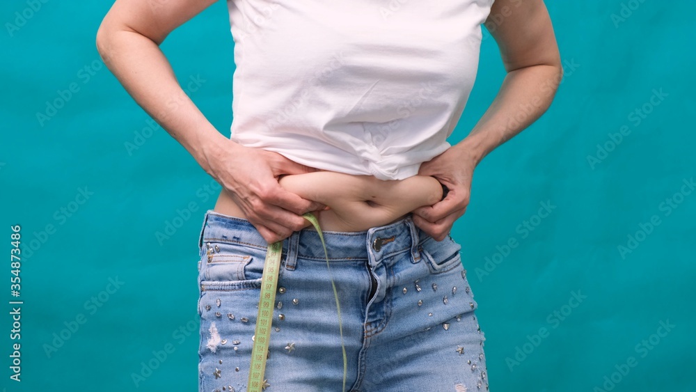 Woman holds a fold of skin on a thick belly, fat female body on a green ...