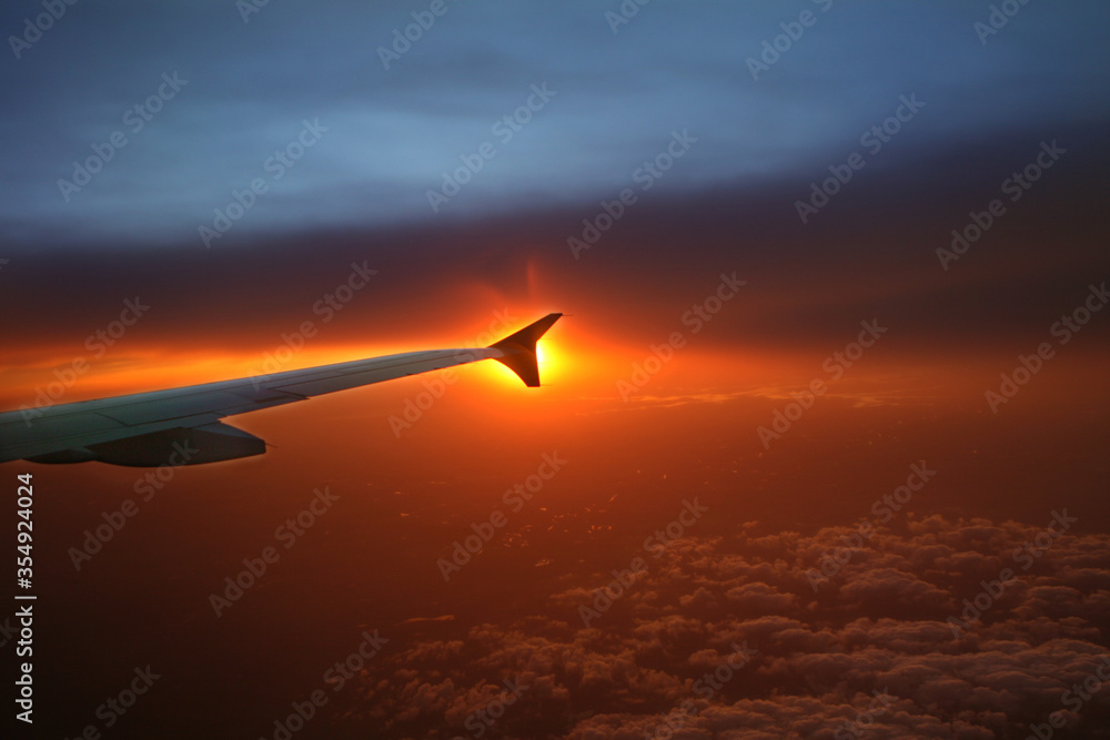 airplane wings in the sunset while flying the sky with red sun on ...