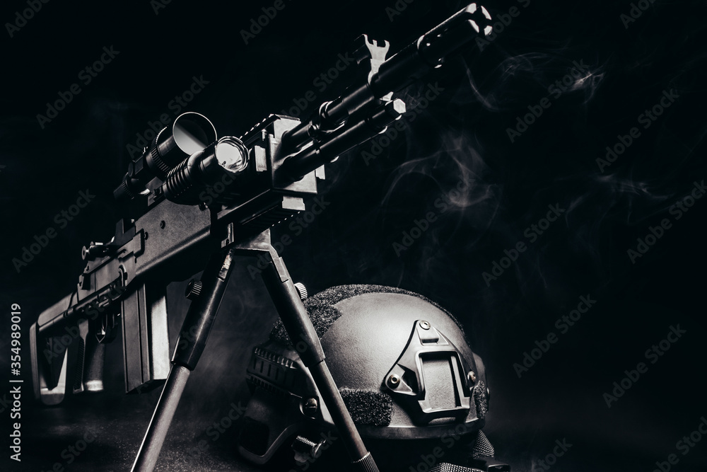 Sniper rifle with scope standing on table with soldier armor helmet on ...