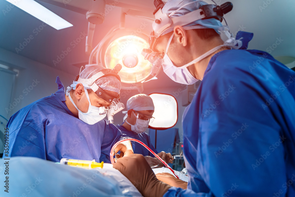 Medical team performing surgical operation in bright modern operating ...