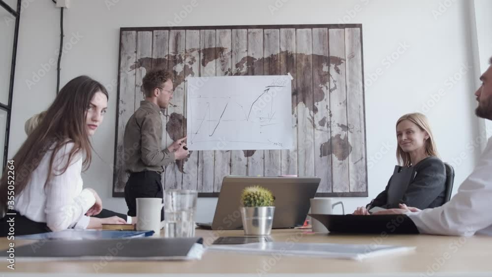 Business people are sitting at the conference table. The man is drawing ...