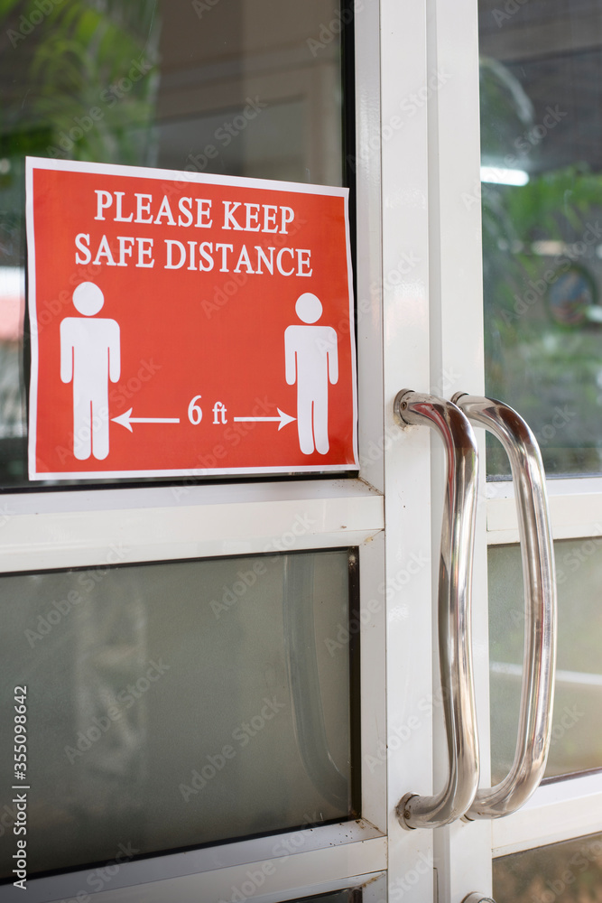Red sign printed "PLEASE KEEP SAFE DISTANCE 6 ft" on the door office ...