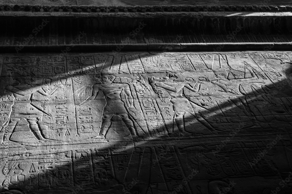 Black and white ancient Egyptian hieroglyphs on a wall illuminated by ...