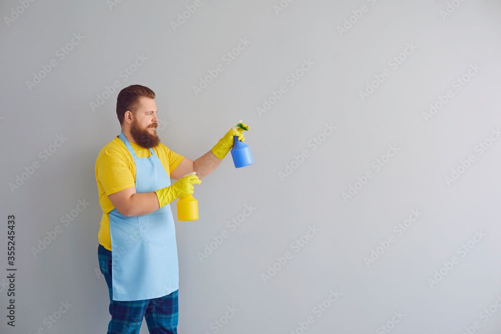 Funny fat man with a beard in an apron cleans up on a gray background ...