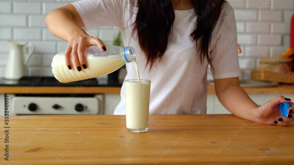 Woman pouring milk into glass. Close up of woman's hands filling ...