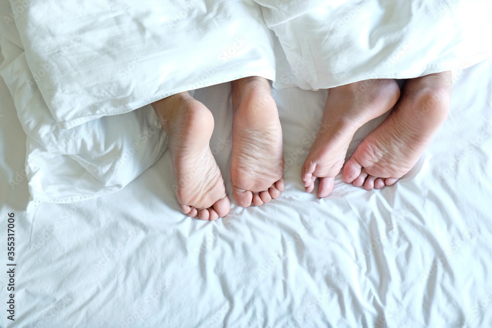 Close-up barefoot of couple on white bed, couple feet in bed under ...