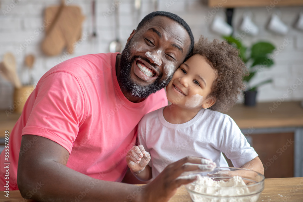 Dark-skinned father looking funny with face stained with flour, his ...