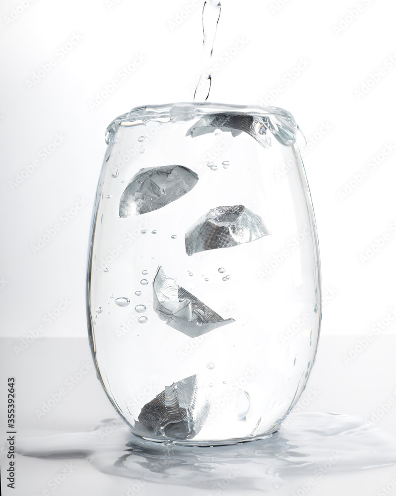 water pouring into glass dripping with silver paper boats floating ...