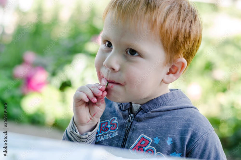 A three-year-old child with red hair eats cherry. The baby's face is ...
