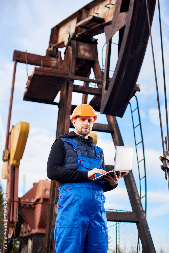 Vertical portrait of oil man, wearing blue overalls and orange helmet ...