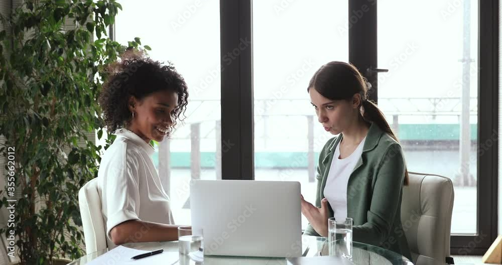 Two african and caucasian young female colleagues team discussing ...