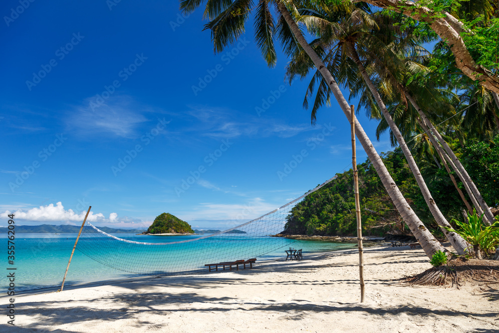 A tropical beach with a beach volleyball court and net. Clear water and ...