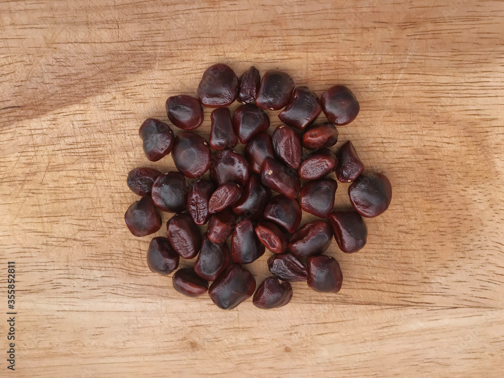 Shiny dark brown roasted tamarind seeds formed in circle on wood chop ...