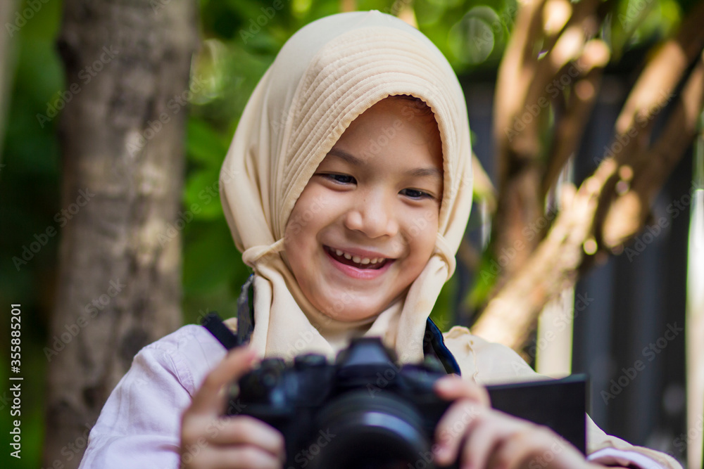 Muslim School kid.Pretty little girl in hijab using camera with happy ...