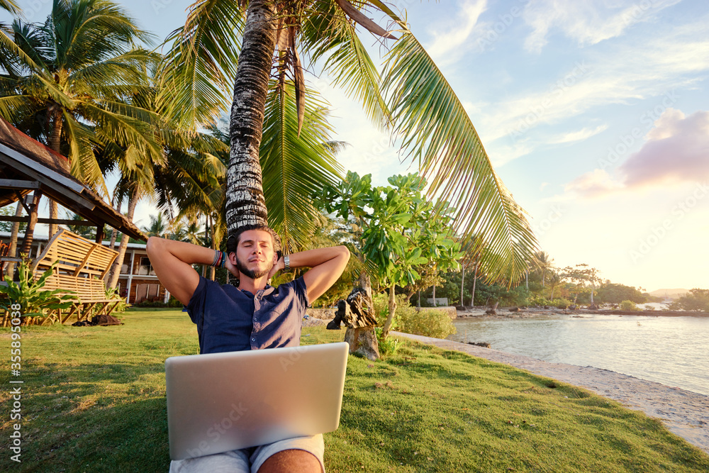 Work and vacation. Young man working on laptop computer on the tropical ...