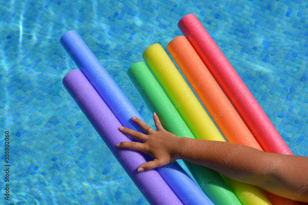 Womanâ€™s arm holding pool noodles in a rainbow colour sequence in a ...