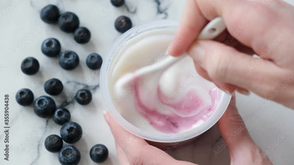 Blueberry greek yogurt in jar. Person stirring blueberry filling with ...