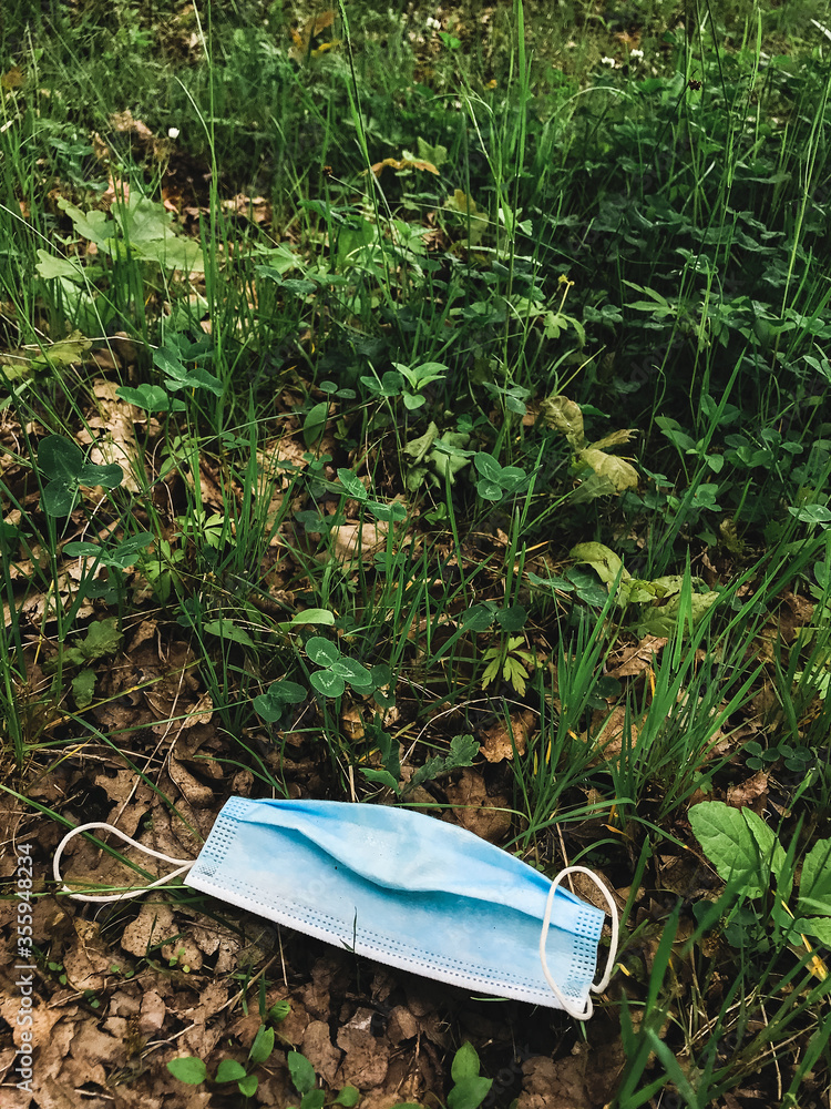 Disposable dirty face mask on ground, single use plastic trash on grass ...