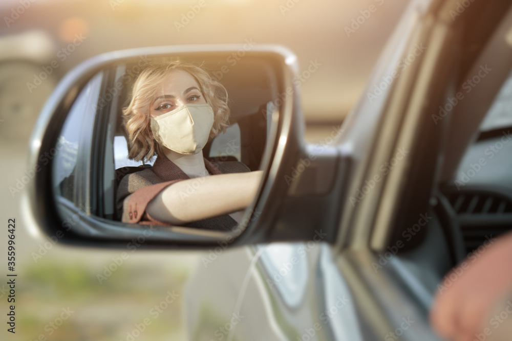 Beautiful girl driver with a mask on her face, sitting at the wheel of ...