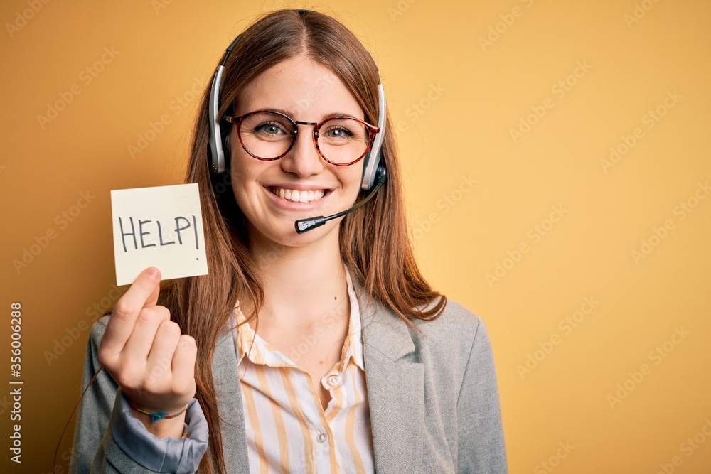 Young redhead call center agent woman overworked using headset holding ...