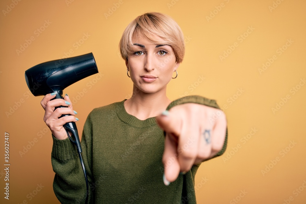 Young blonde woman with short hair drying her hair using hairdryer over ...