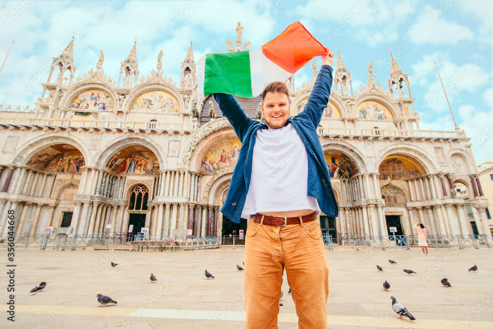 young smiling man holding italian flag above his head in font of saint ...