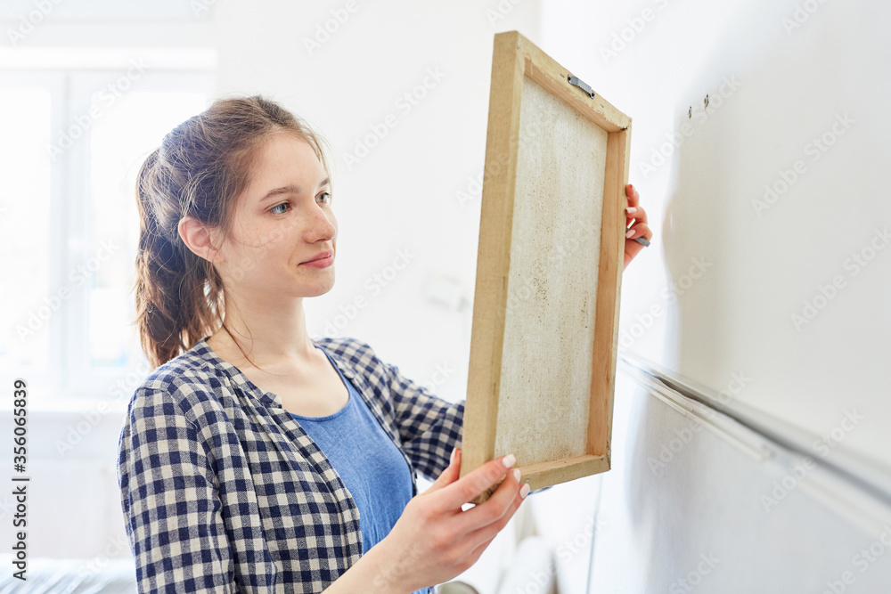 Junge Frau hängt ein Bild an der Wand auf Stock Photo | Adobe Stock