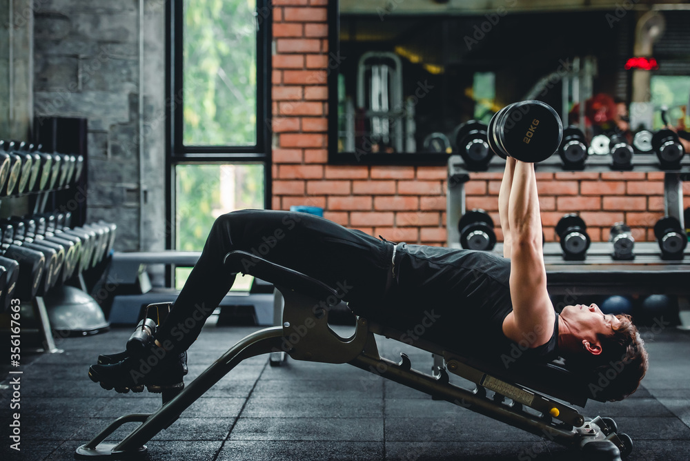A handsome Asian man is exercising his chest by pushing a bench with a ...