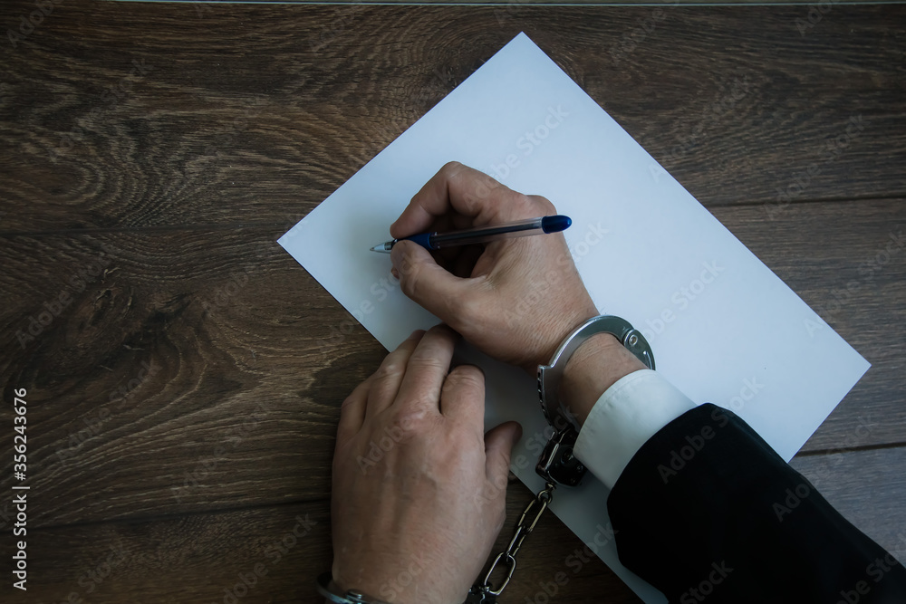 Hands of a man in handcuffs hold a fountain pen in front of a blank ...