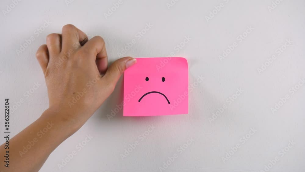 Woman's hand sticking note with a sad face emoticon over a white ...