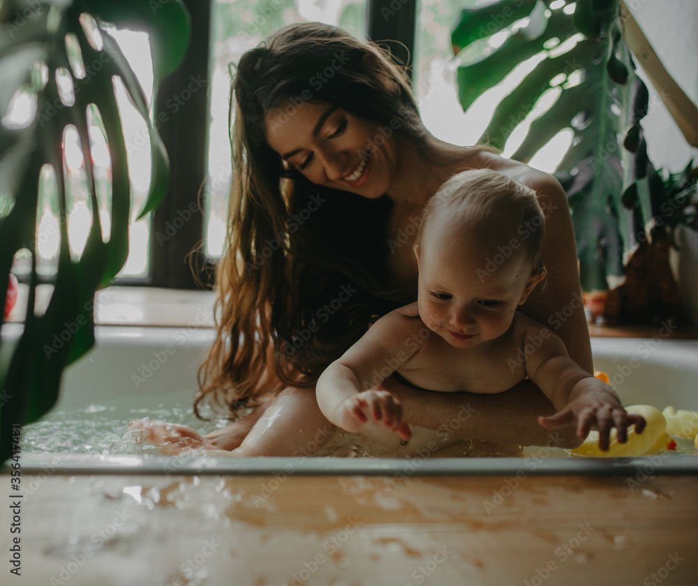 Mother with her baby bathe in bathtub and play with floating toys ...