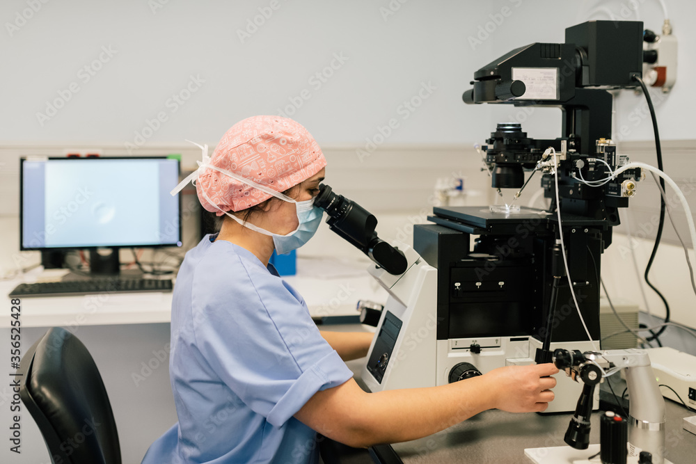 Side view of woman in medical uniform and mask using modern machine to ...