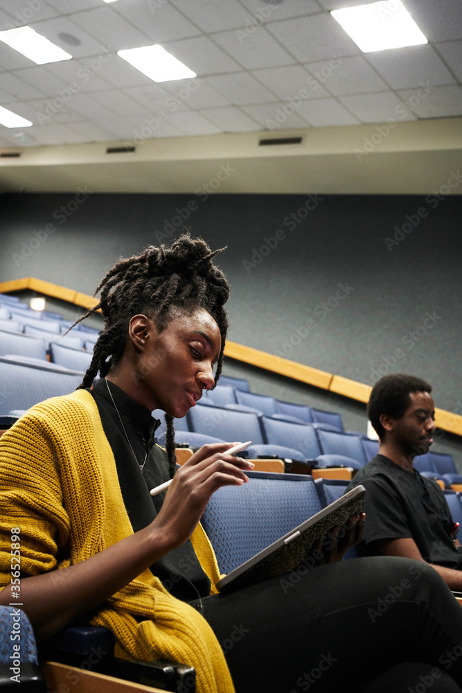 From below black woman with dreadlocks smiling and using tablet while ...