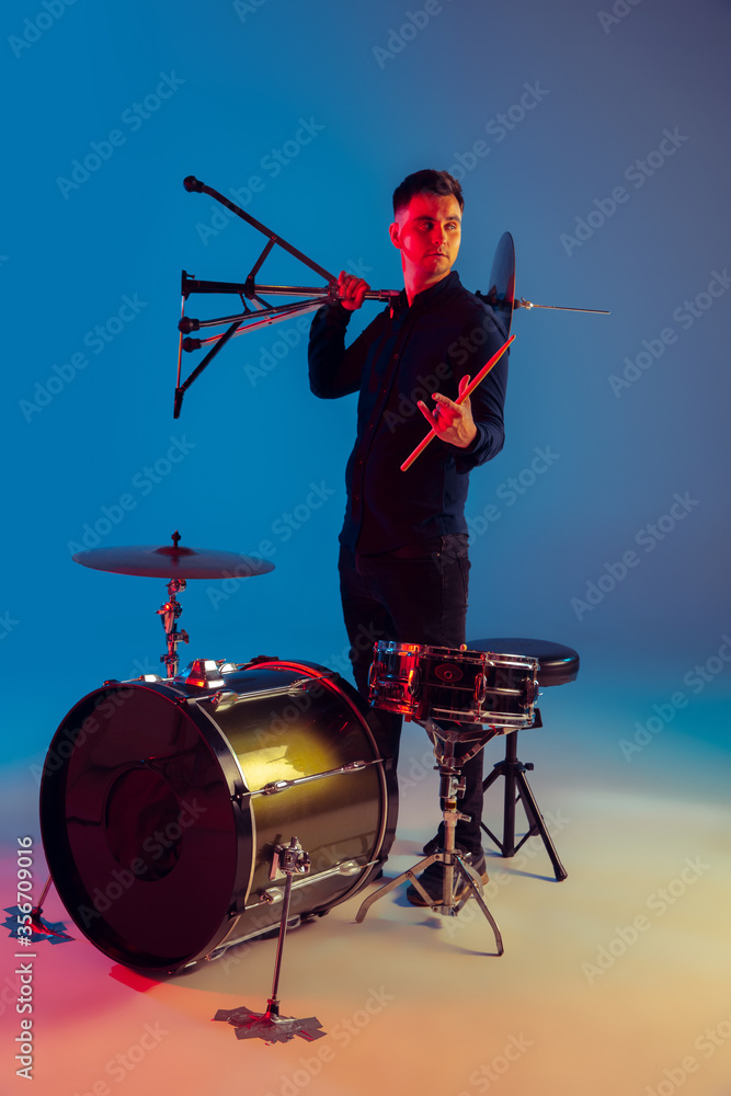 Caucasian male drummer improvising isolated on blue studio background in neon light. Performing ...