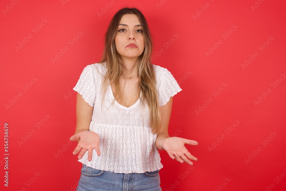 Puzzled and clueless young woman with arms out, shrugging her shoulders ...
