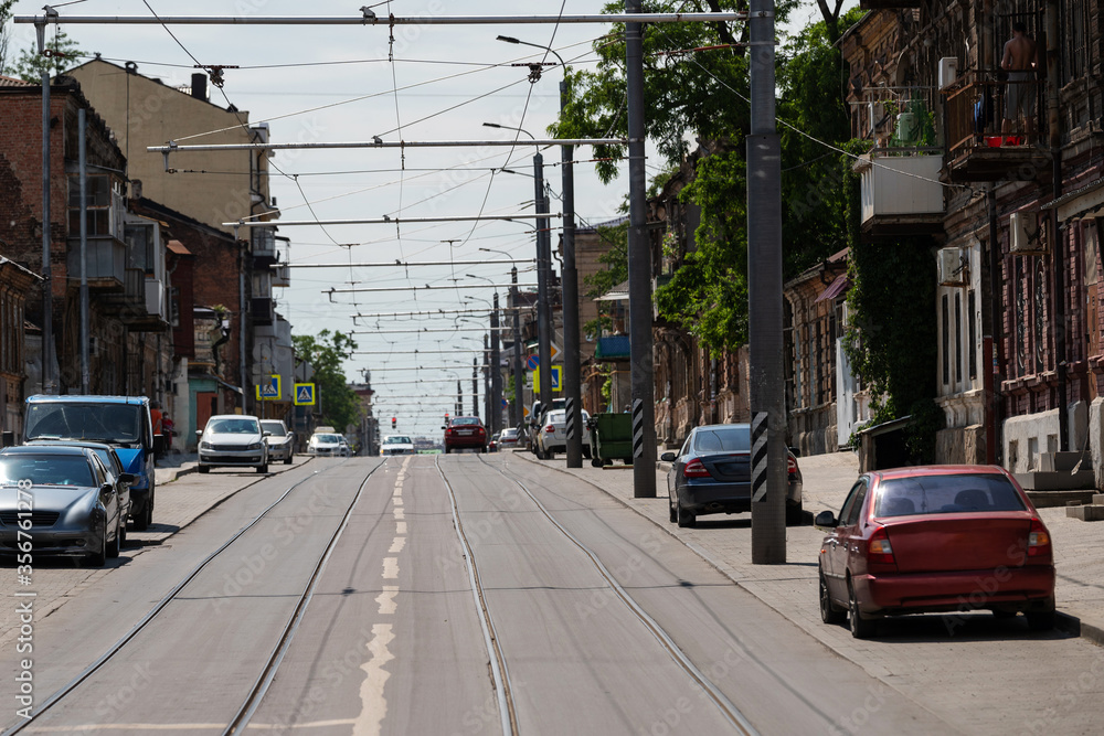 metal rails for a tram on a road on a city street with parked cars and ...