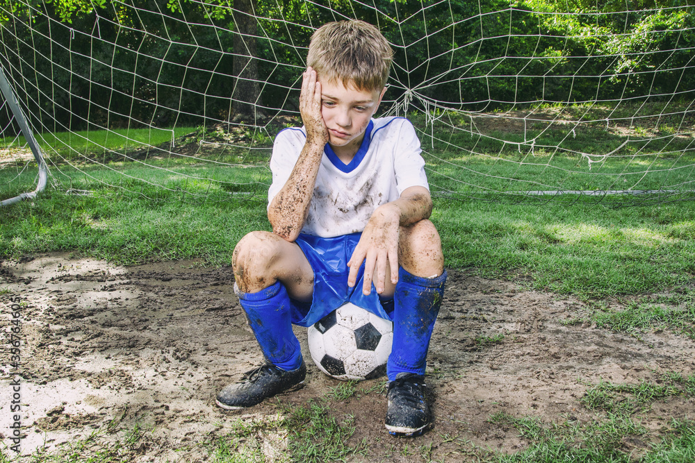 Little muddy soccer boy sitting unhappy in front of goal Stock Photo ...