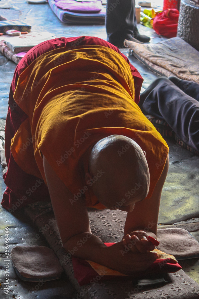 An old bold monk wearing traditional red and yellow cloathes praying in ...