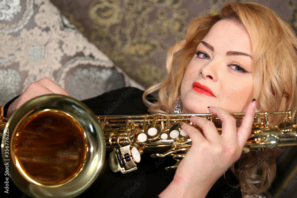 Portrait of a charming blonde with a saxophone in her hands. Beautiful ...